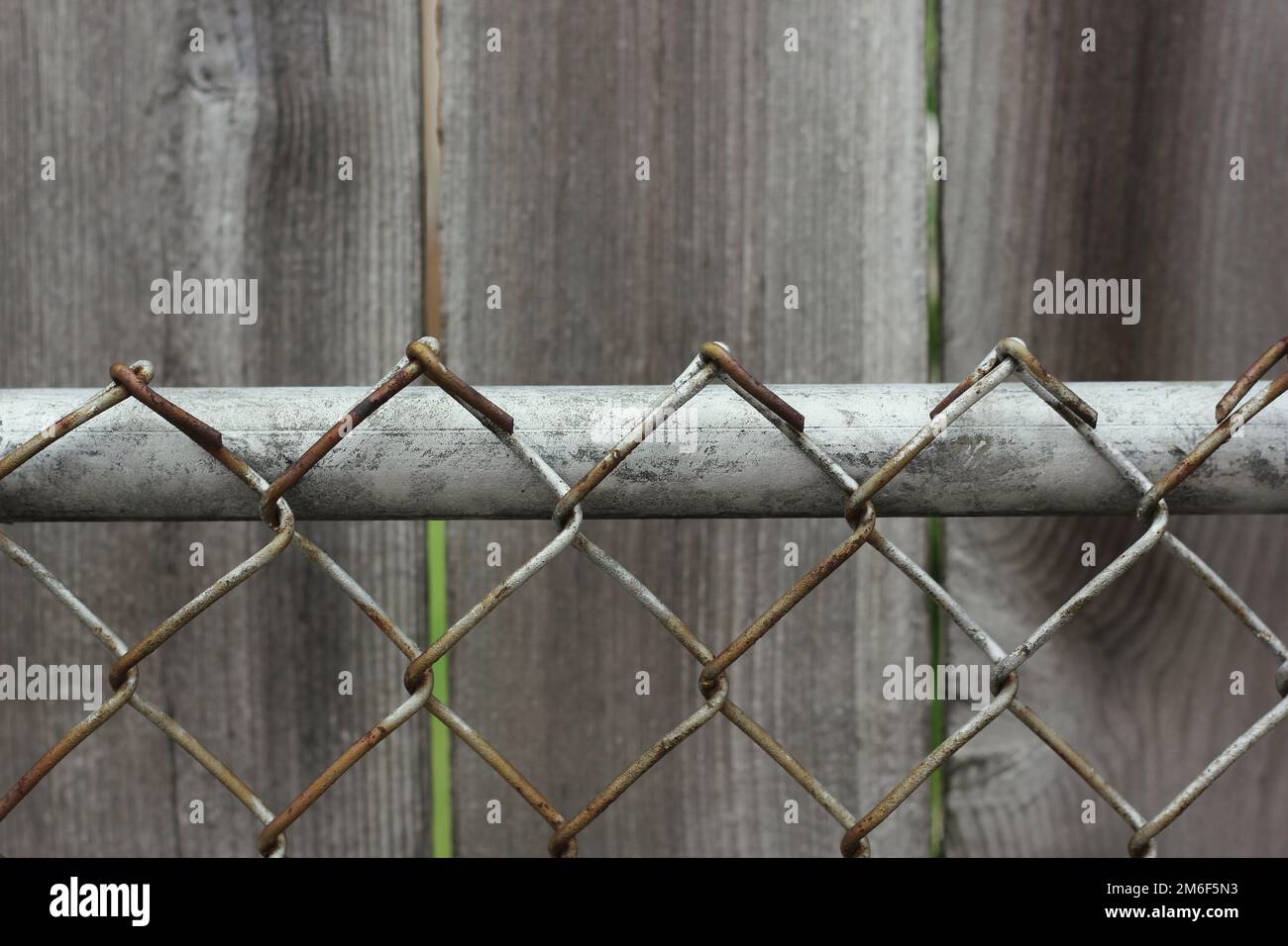 Typical and common metal chain link fence running along a gray wooden ...