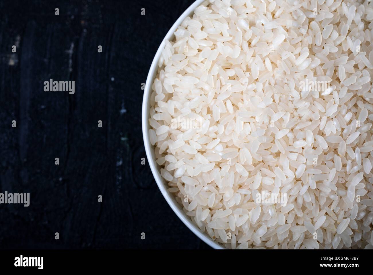 Bowl containing uncooked white rice on a black background. Top view ...