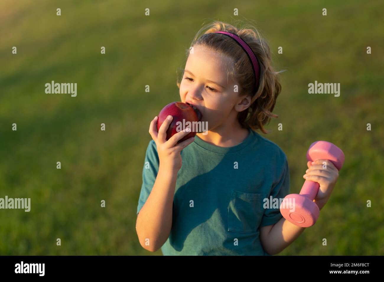 Sporty kid with apple and dumbbell outdoor in summer park. Kid boy ...