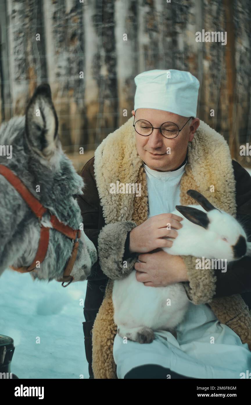 Caring doctor veterinarian holds a rabbit in his arms and a donkey next ...