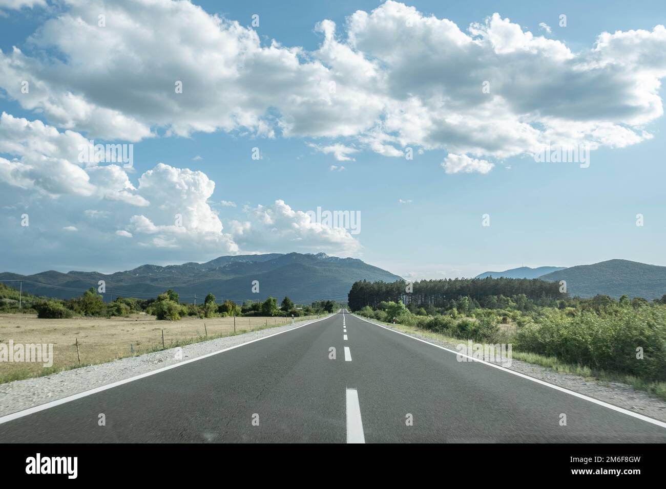 A view of the open country road with a bright blue sky and mountains n ...