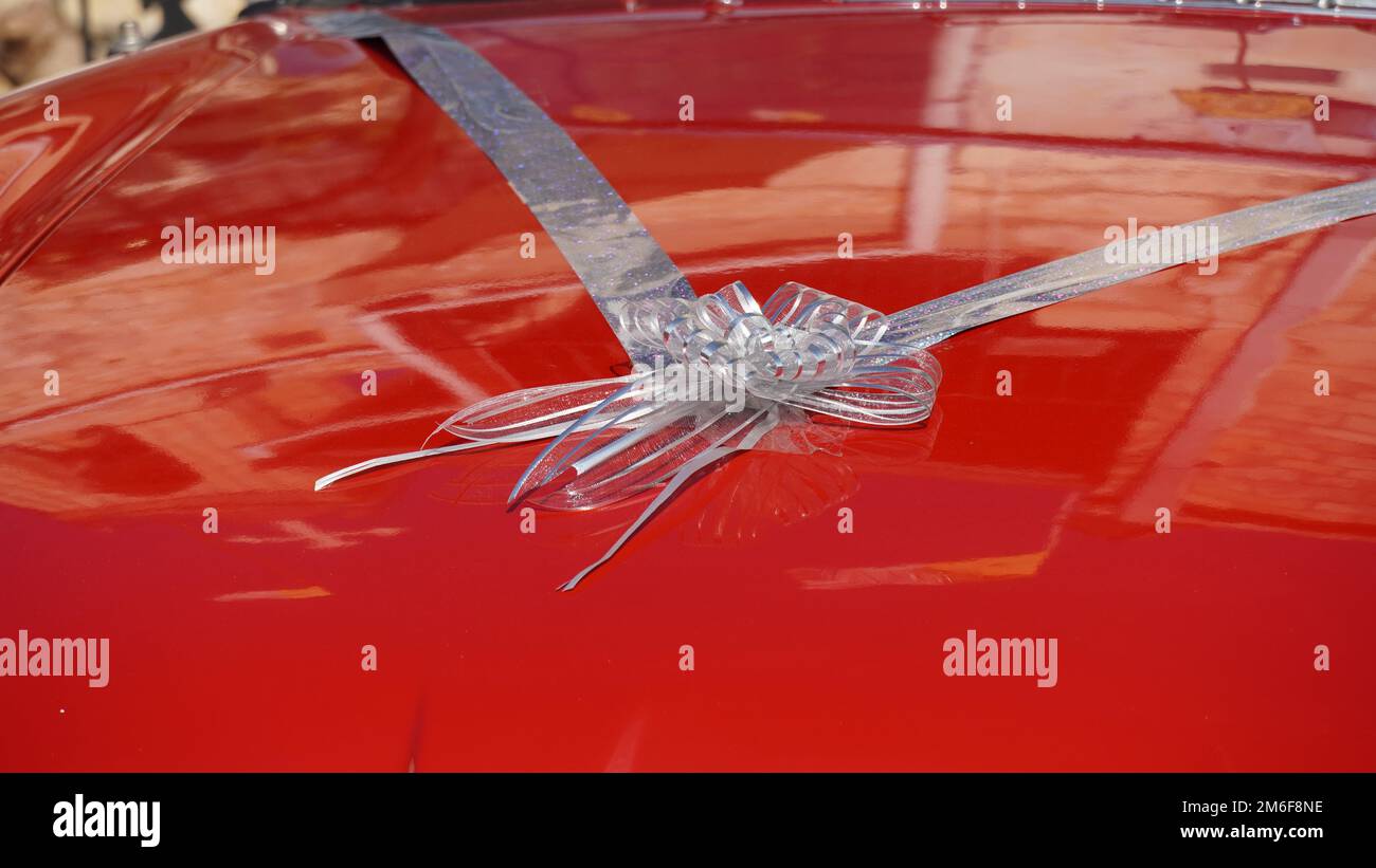 Red hood of Retro classic wedding car decorated with silver ribbon ...