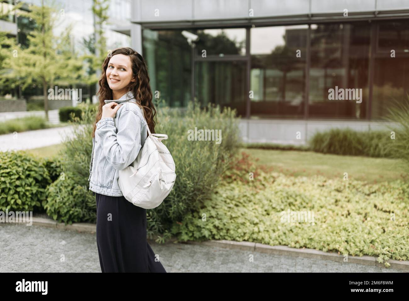 Happy pretty young brunette woman with white nylon backpack in blue ...