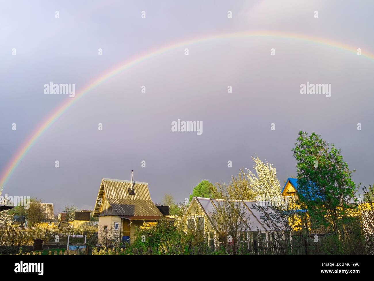 Rainbow over the roofs of rural houses in the stormy evening sky after ...