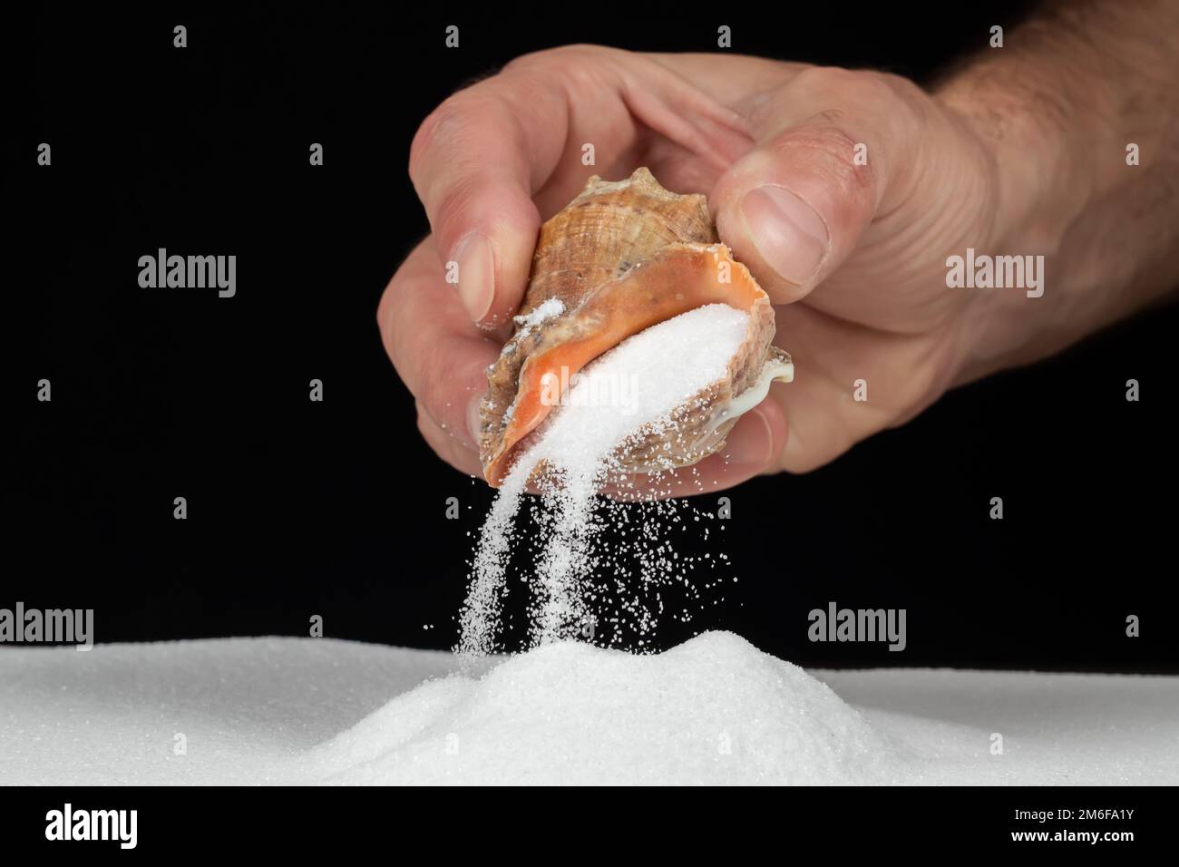 sand pouring out of sea shells on black background Stock Photo - Alamy