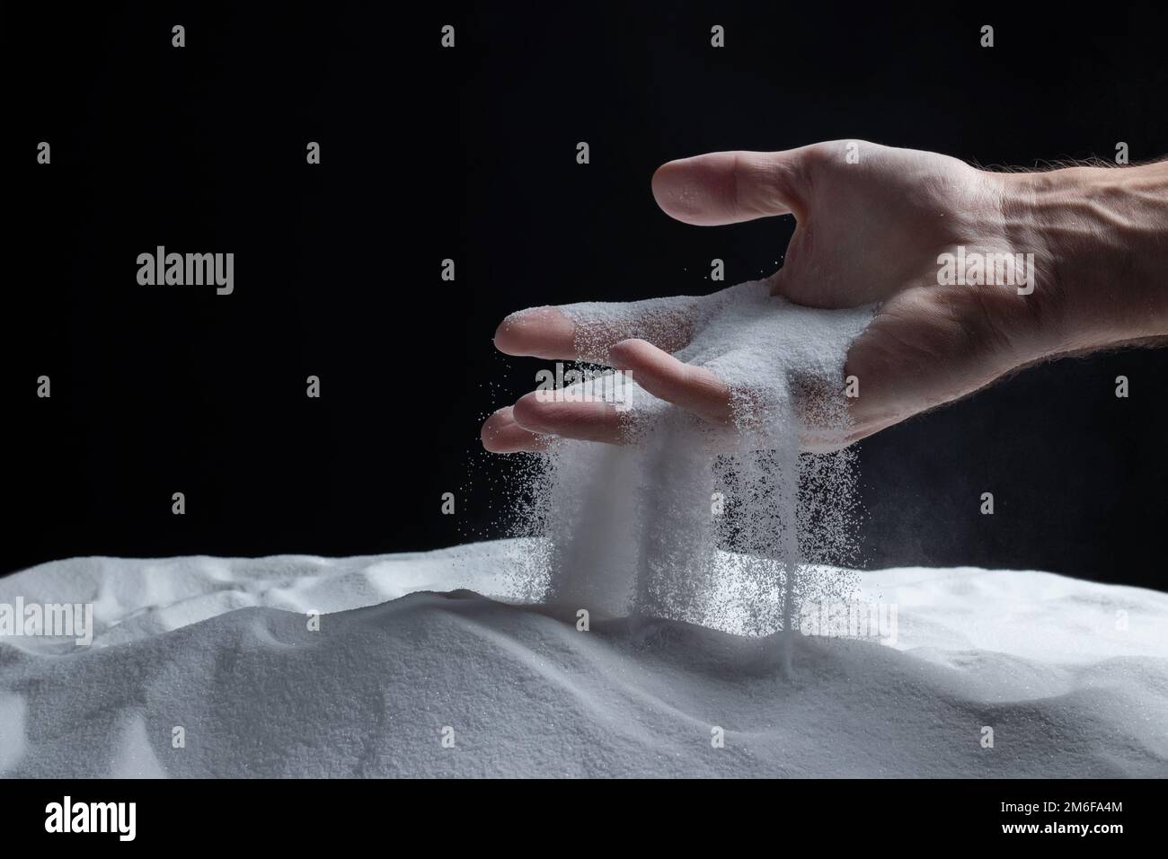 Man with handful of white dry sand in her hands, spilling sand through ...