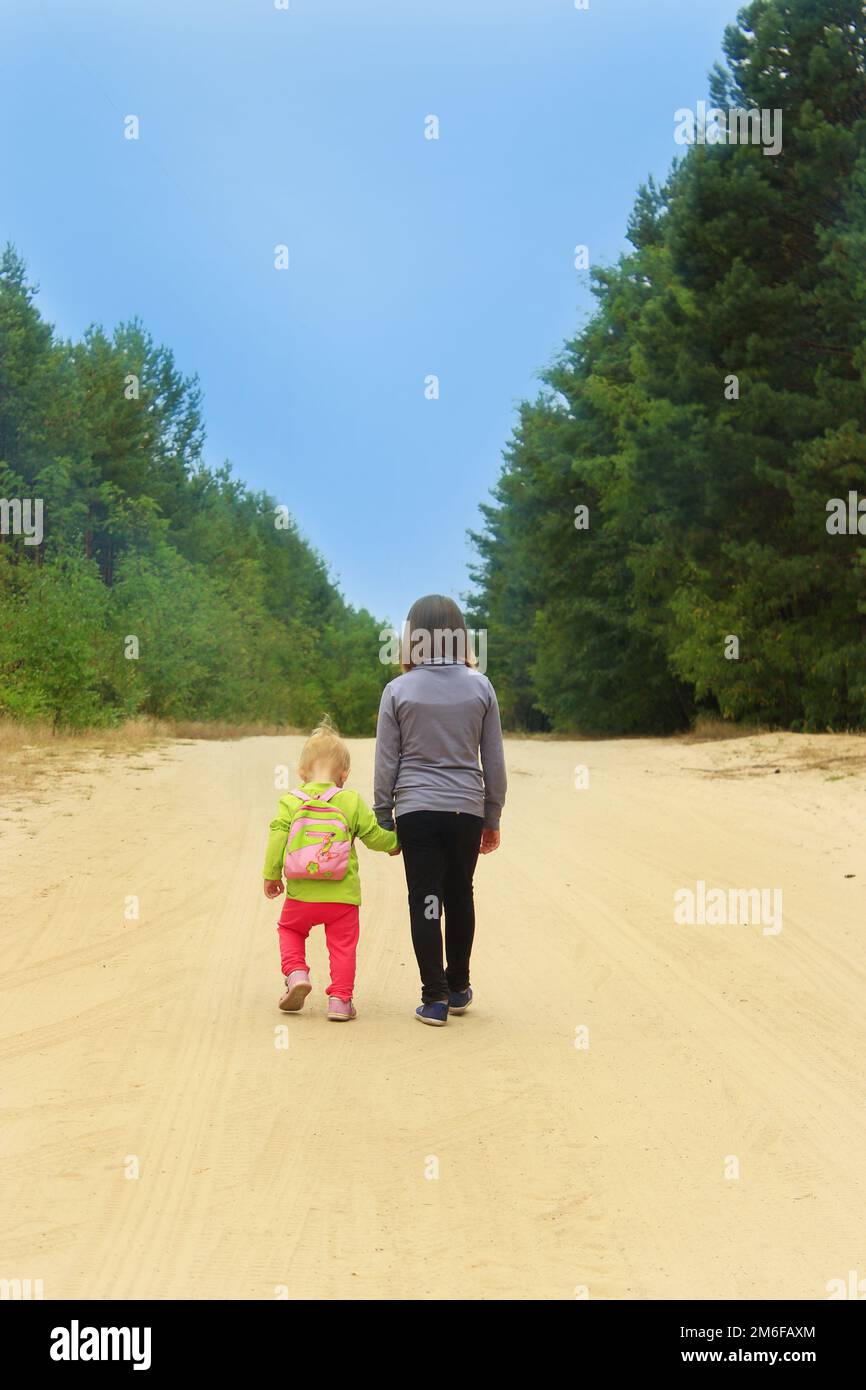 Little tourists go on road. Girls travellers walk on the forest path ...