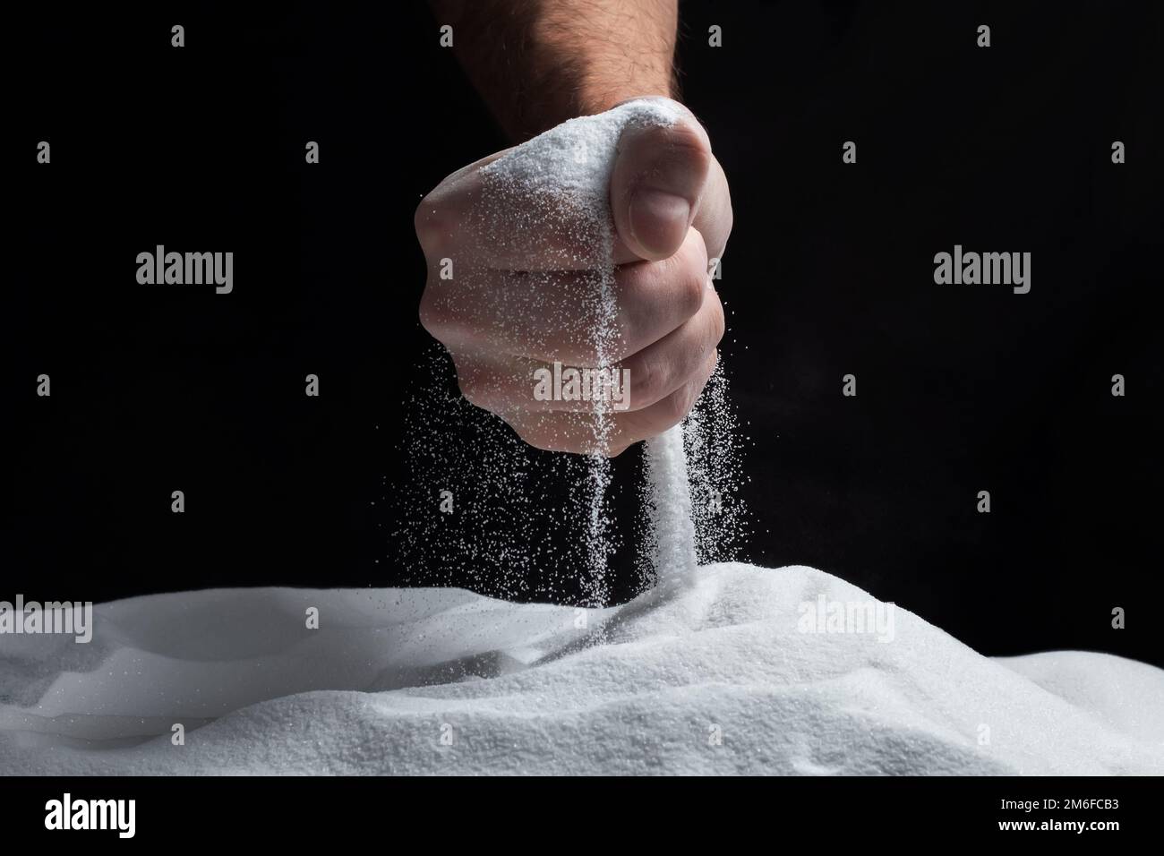 Man with handful of white dry sand in her hands, spilling sand through ...