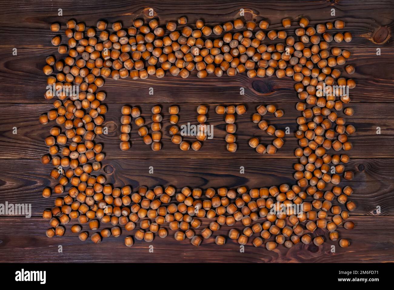 Frame of hazelnuts with shells on brown wooden boards. The word nuts is ...