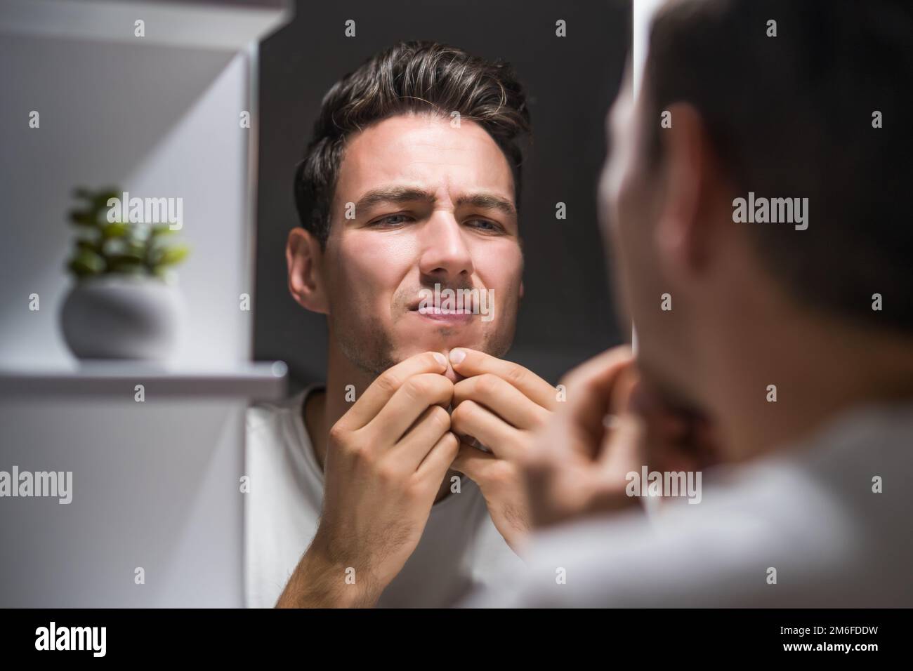 Man squeezing pimple while looking himself in the mirror Stock Photo ...