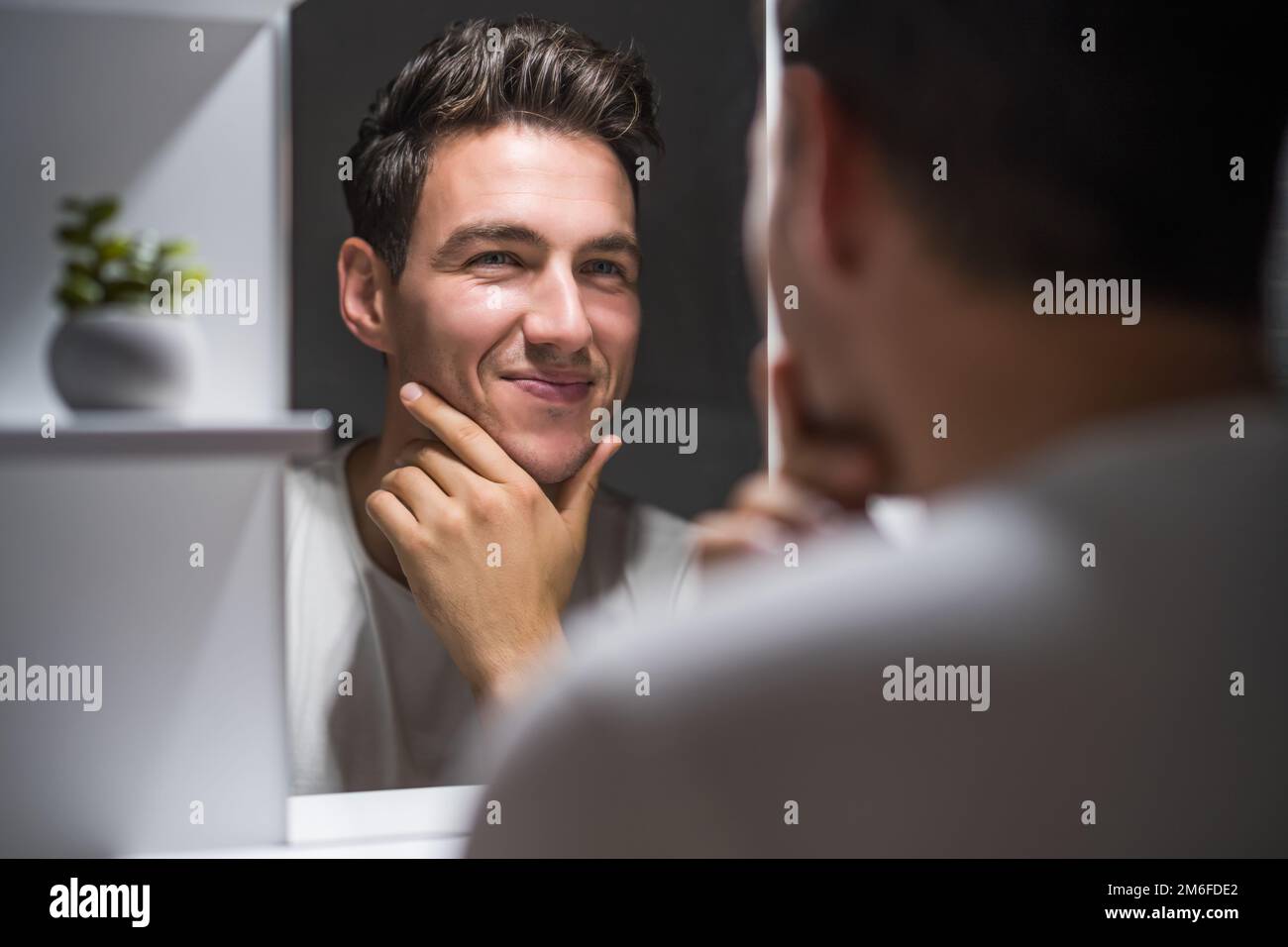 Portrait of man looking himself in a mirror while standing in bathroom ...