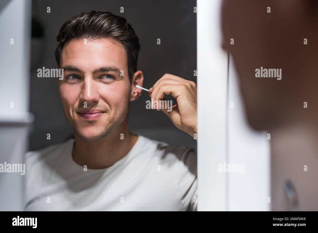 Man cleaning ear while looking himself in the mirror Stock Photo - Alamy