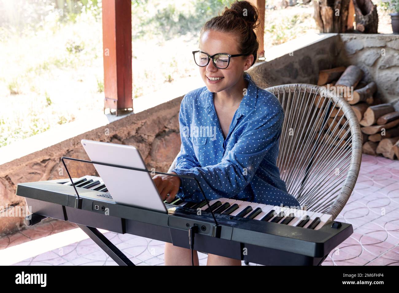 Young woman in glasses playing electric piano on terrace using digital ...