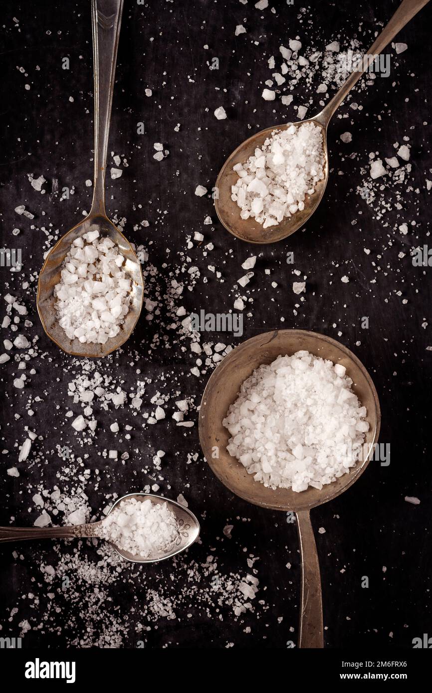 Top view of four spoons with coarse grained sea salt on black ...