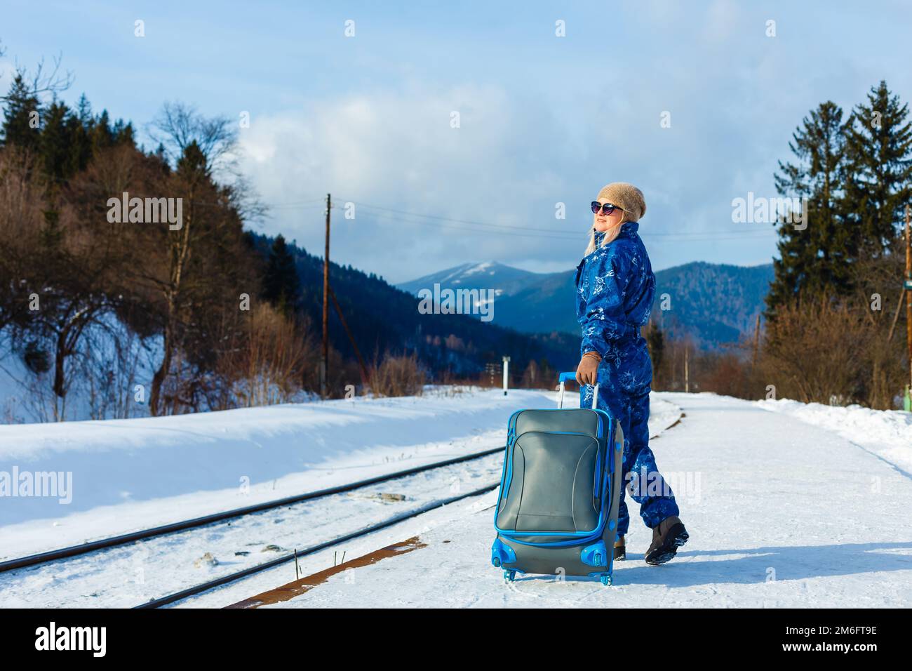 Woman pulling heavy luggage at a snow train station. Travelling by ...