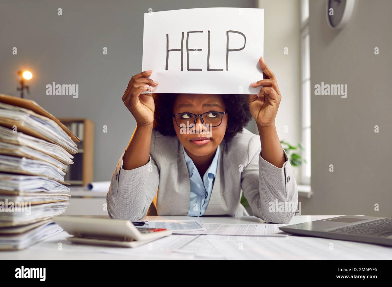 Tired, busy woman sitting at an office desk with paperwork and holding a HELP sign Stock Photo ...