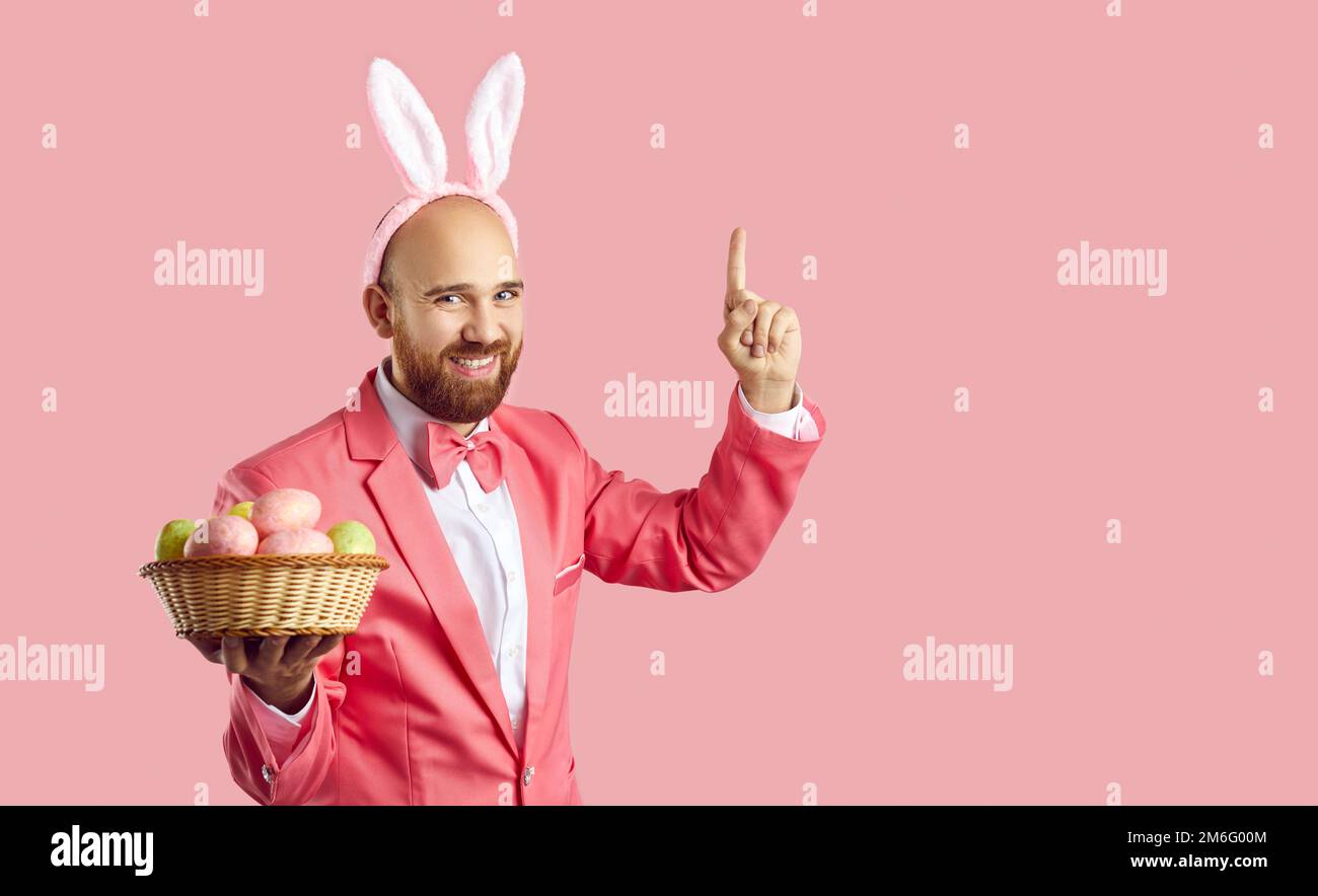 Funny man wearing bunny ears holding Easter eggs, smiling and pointing ...