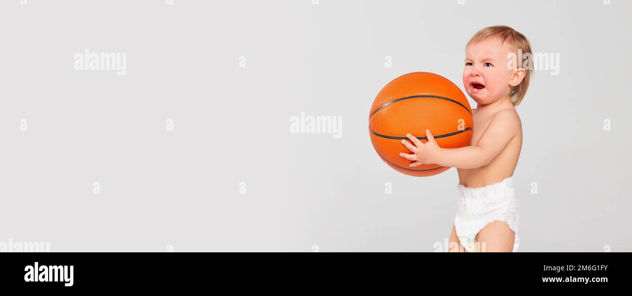 Crying baby with big basketball ball. One little cute toddler girl ...