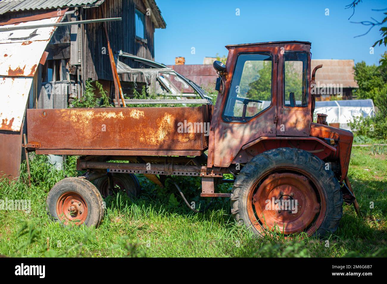 An old rusty tractor stands near the barn on the green grass during ...
