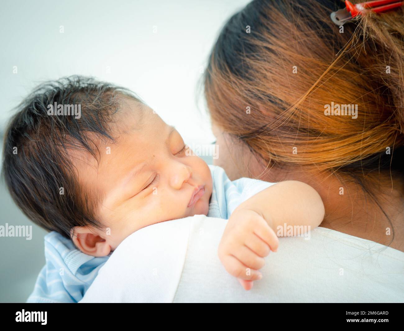 Loving mom carrying her sleeping newborn baby on her shoulder at home.Portrait of mum holding ...