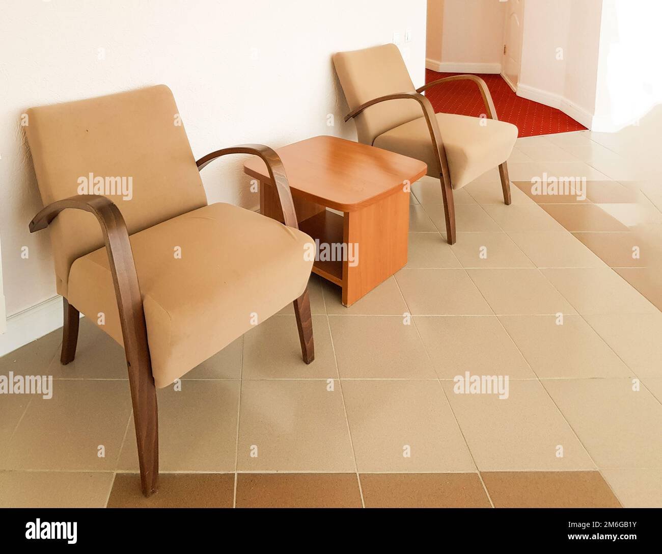 Two brown armchairs and a coffee table between them against a pink wall ...