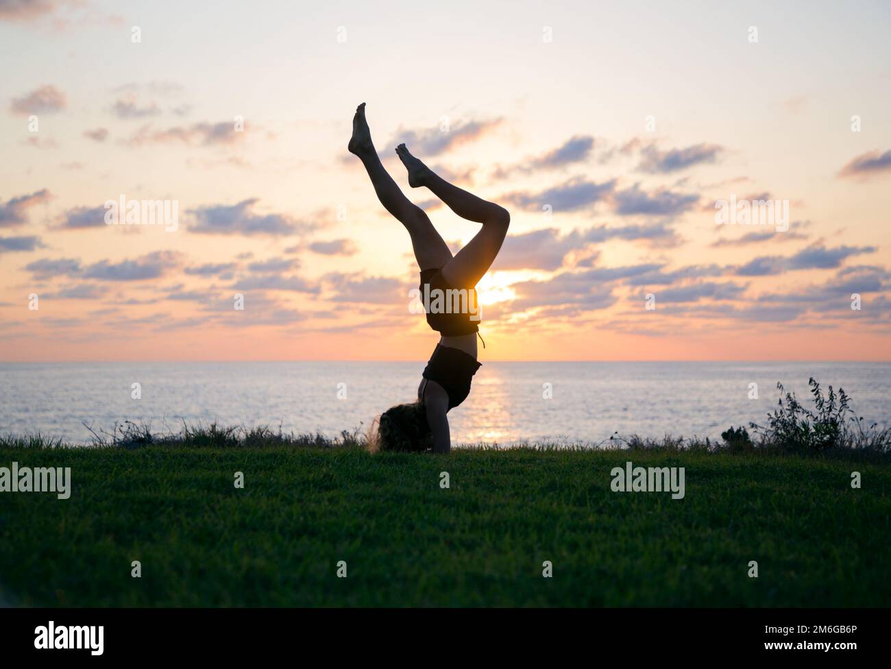 young slender girl teenager does handstand at sunset against of sea ...