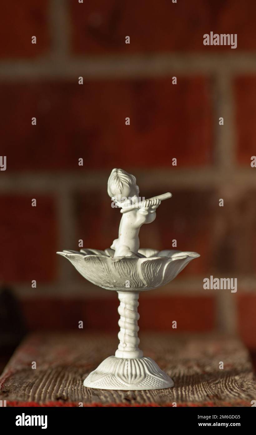 See a closeup of a flute player posed on a floral pedestal with a brick ...