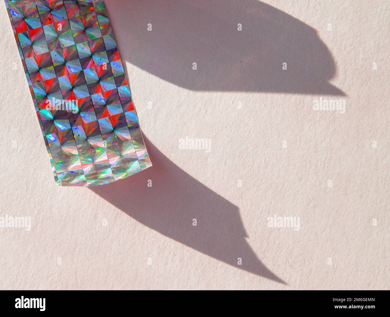 A piece of holographic foil on a white background, hard shadows from ...