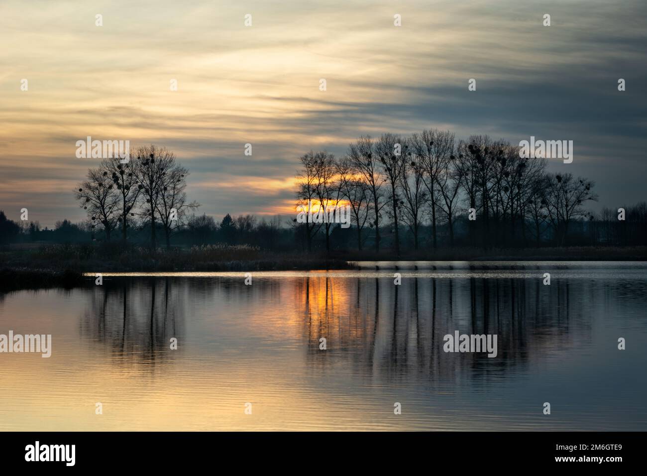 The sun behind the clouds and the reflection of trees in the water ...