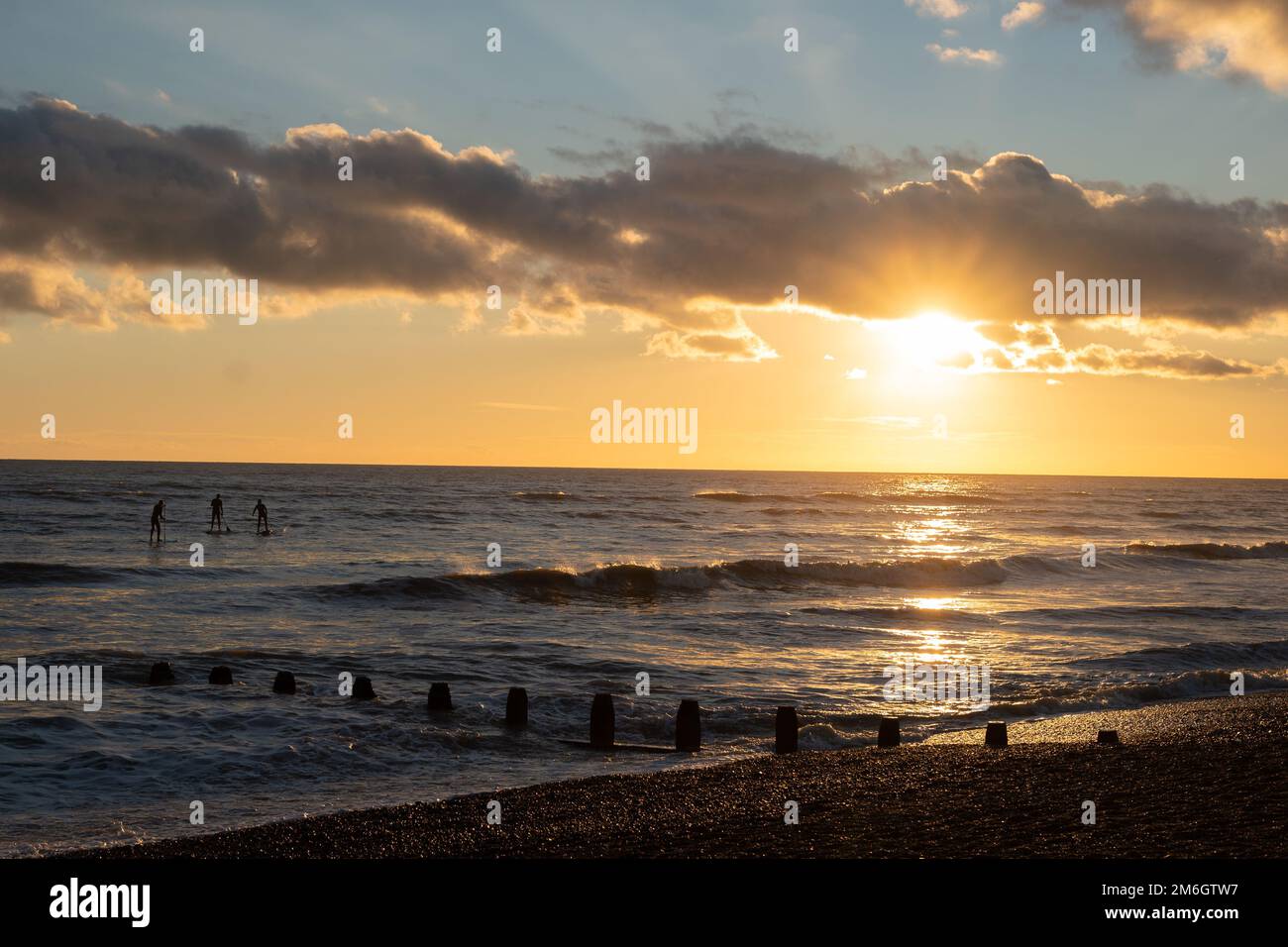 Three surfers in the sea at sunset in the coastal town of Shoreham in ...