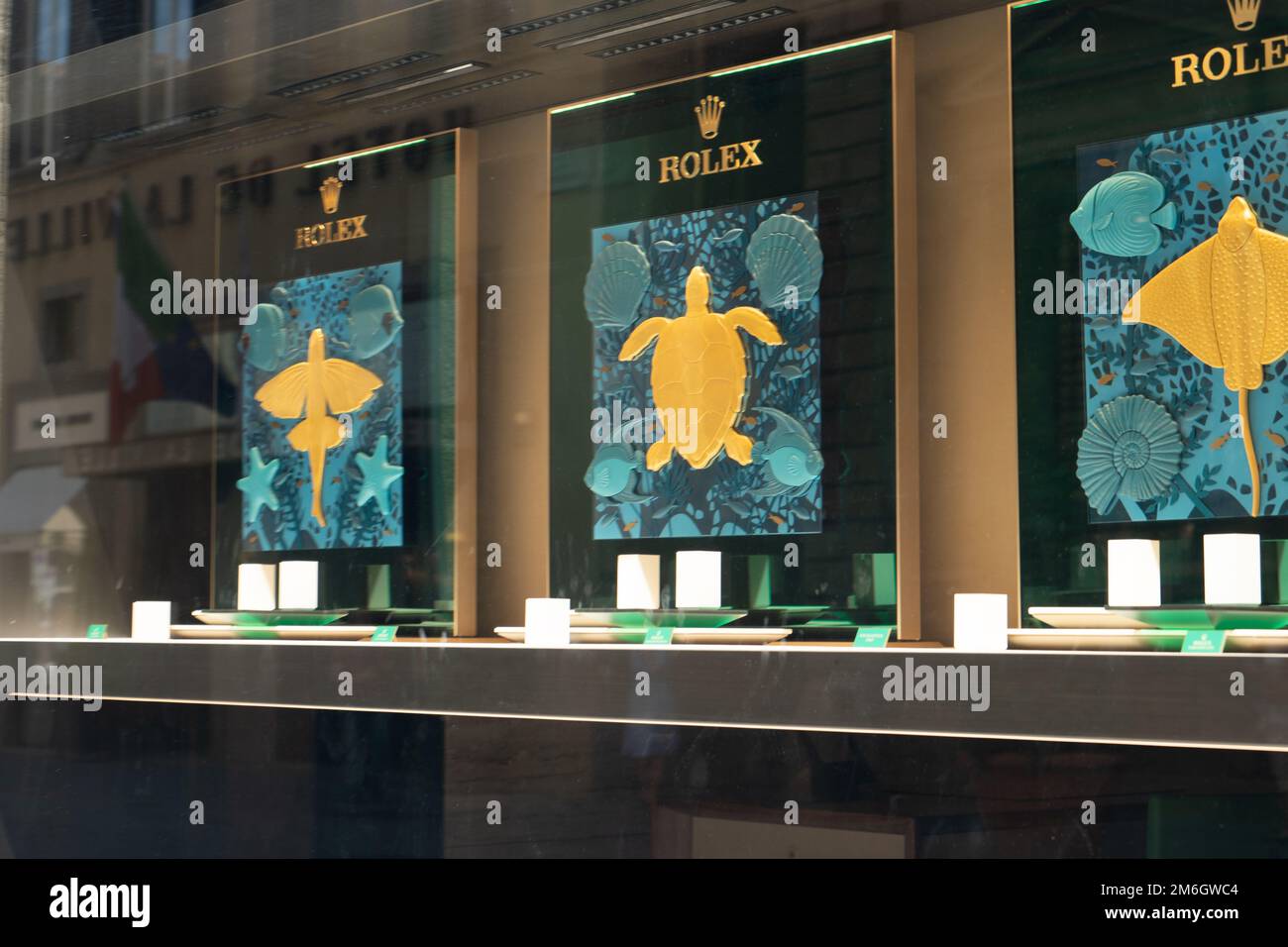 A street view behind a transparent window with Rolex store on the wall ...