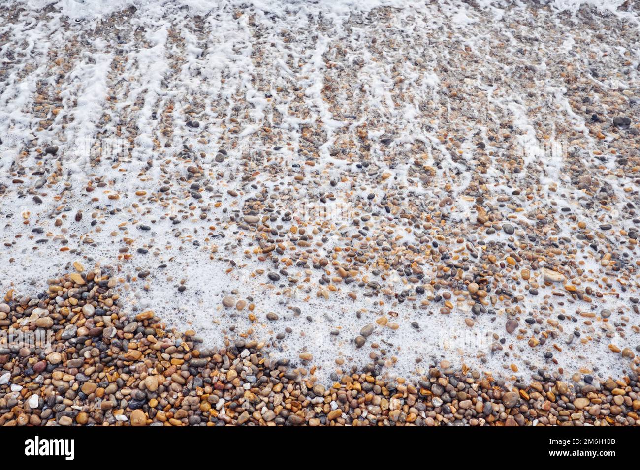 A close up as the foamy sea surf washes up over a people beach on the ...