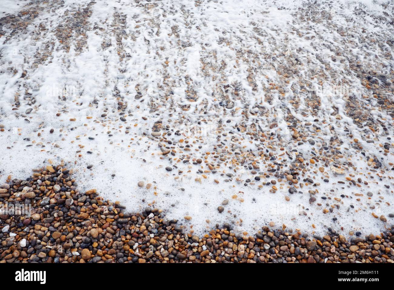 A close up as the foamy sea surf washes up over a people beach on the ...