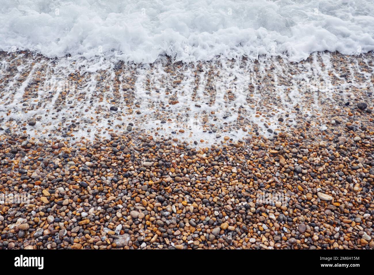 A close up as the foamy sea surf washes up over a people beach on the ...