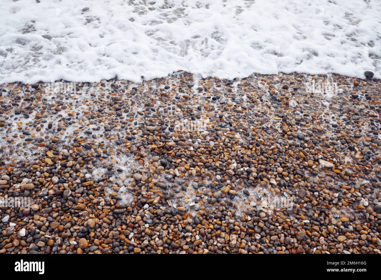 A close up as the foamy sea surf washes up over a people beach on the ...