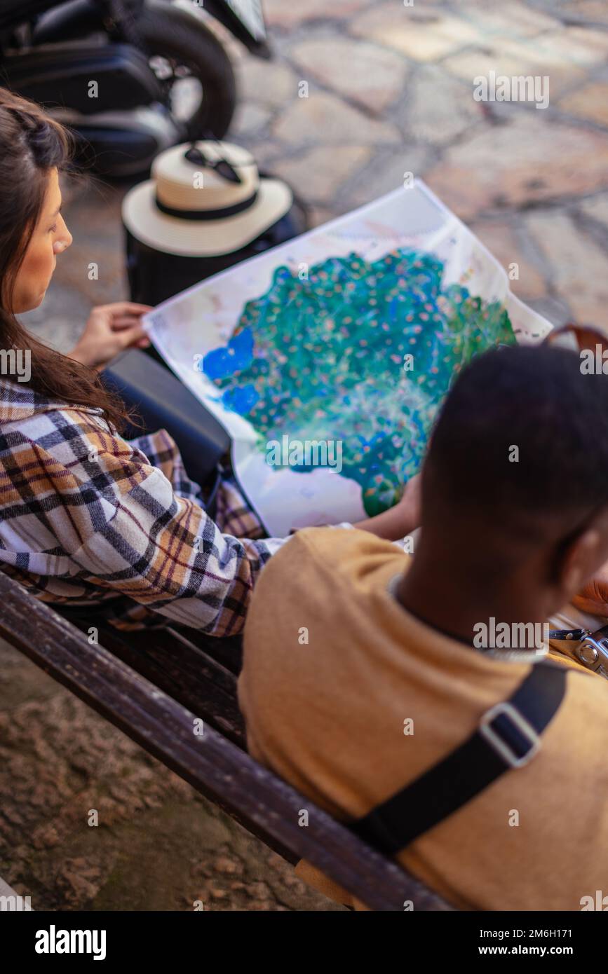 Two tourists are sitting on a bench, taking pictures, looking at the ...