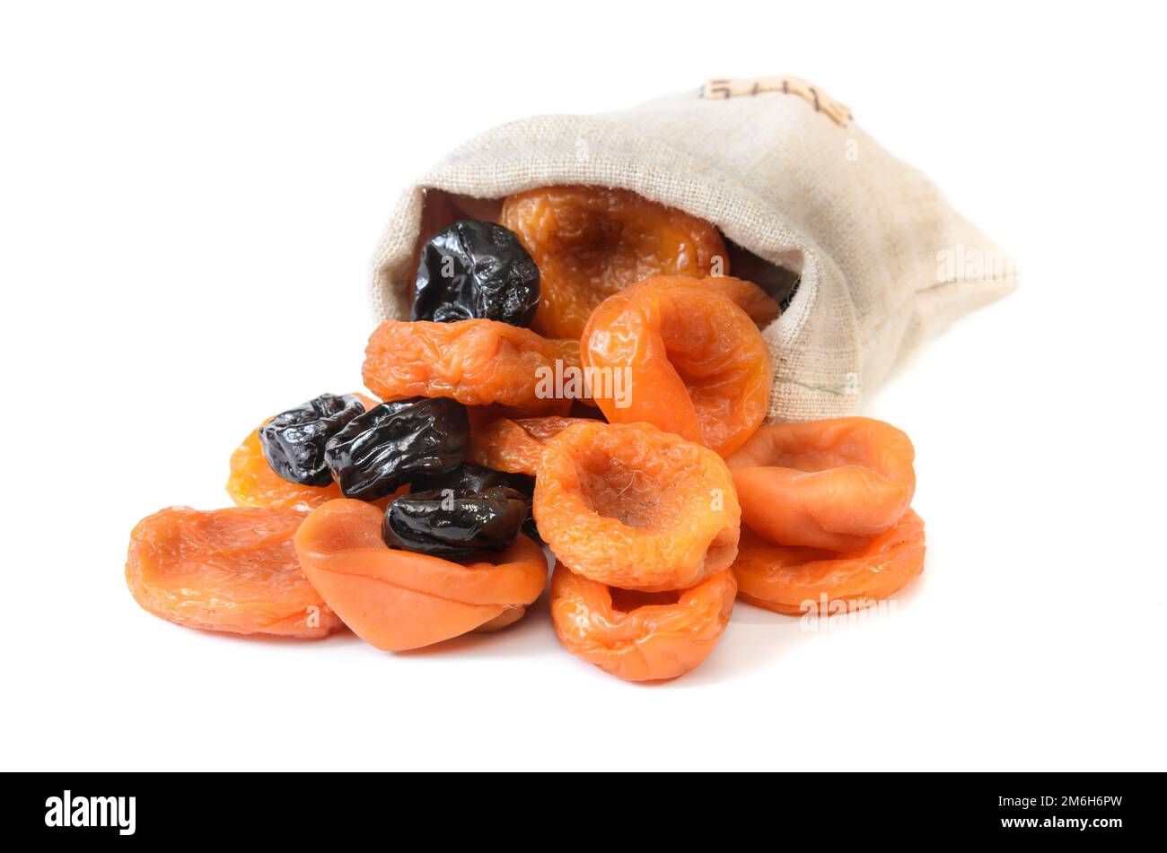 Dried apricots and prunes in a woven bag on a white background with ...
