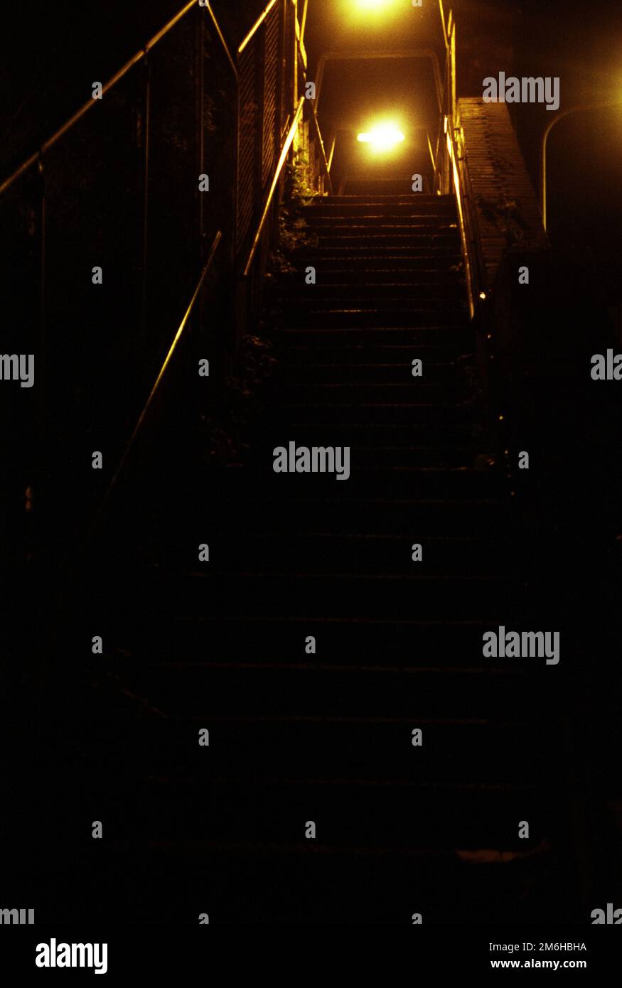 looking up at a flight of stairs to an overpass at night lit from above ...