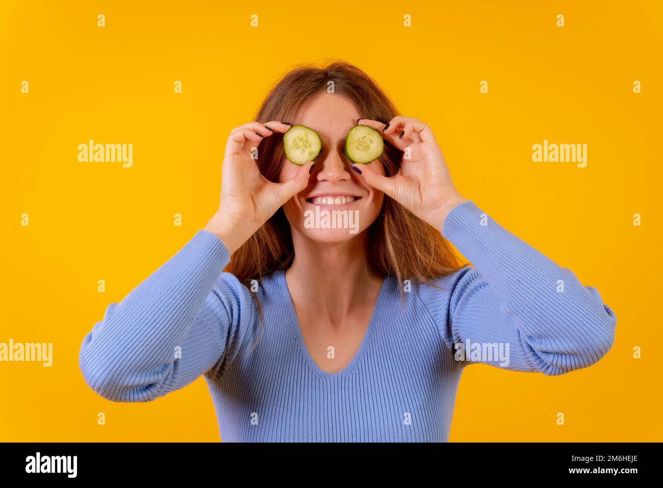 Vegan woman with cucumber slices on her eyes on a yellow background ...