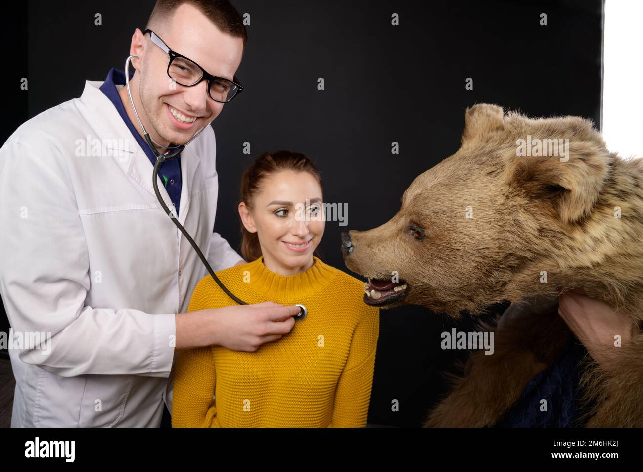 Smiling young man doctor with stethoscope and patient examining bear ...