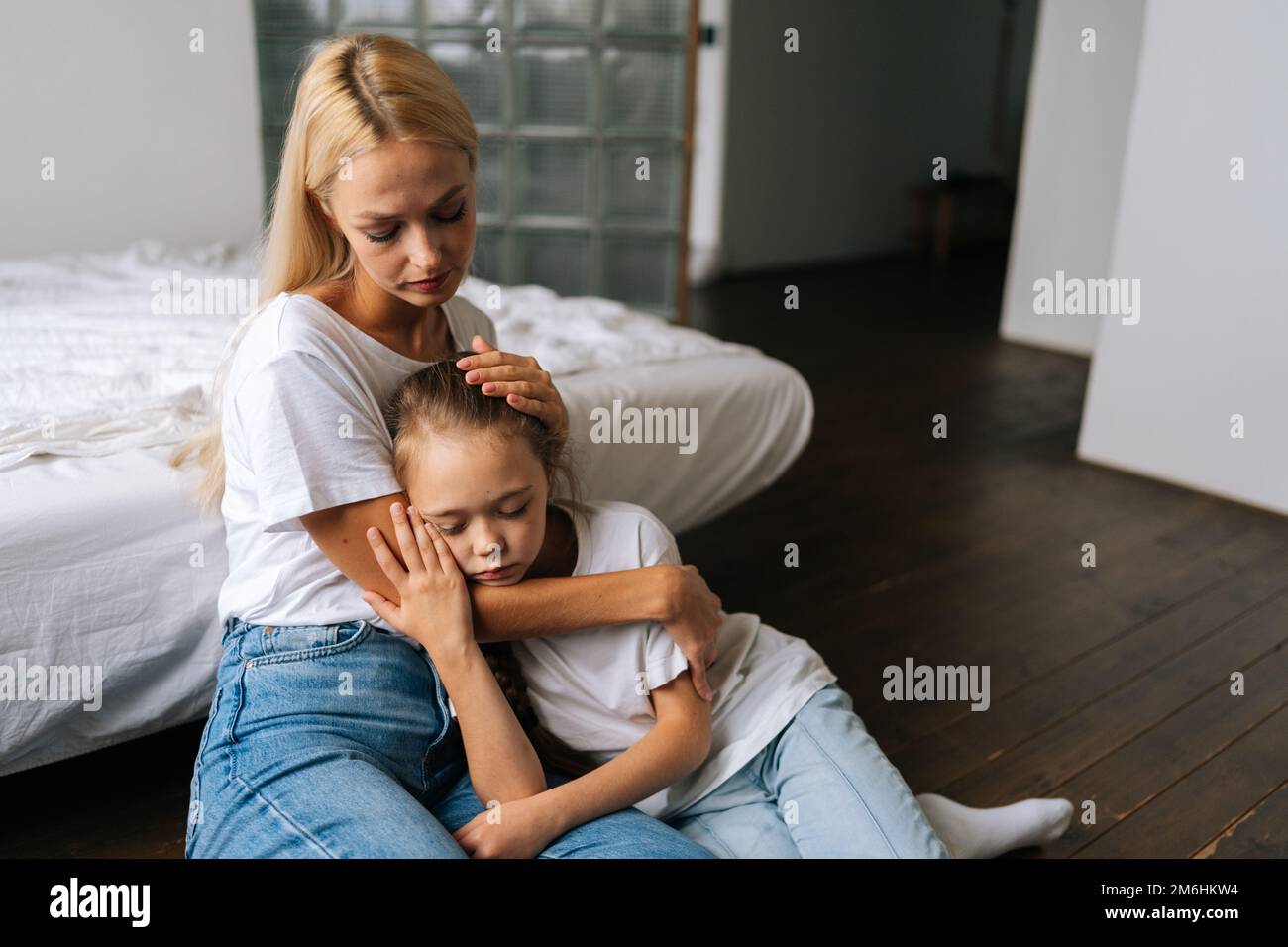 Portrait of tired cute little girl with closed eyes and loving caring mother comforting offended ...