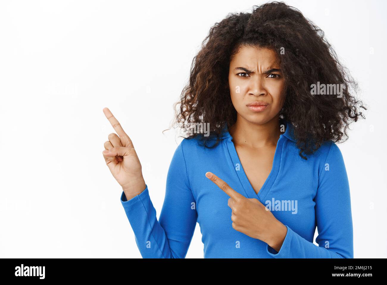 Disappointed girl with curly hair, pointing finger left, showing ...