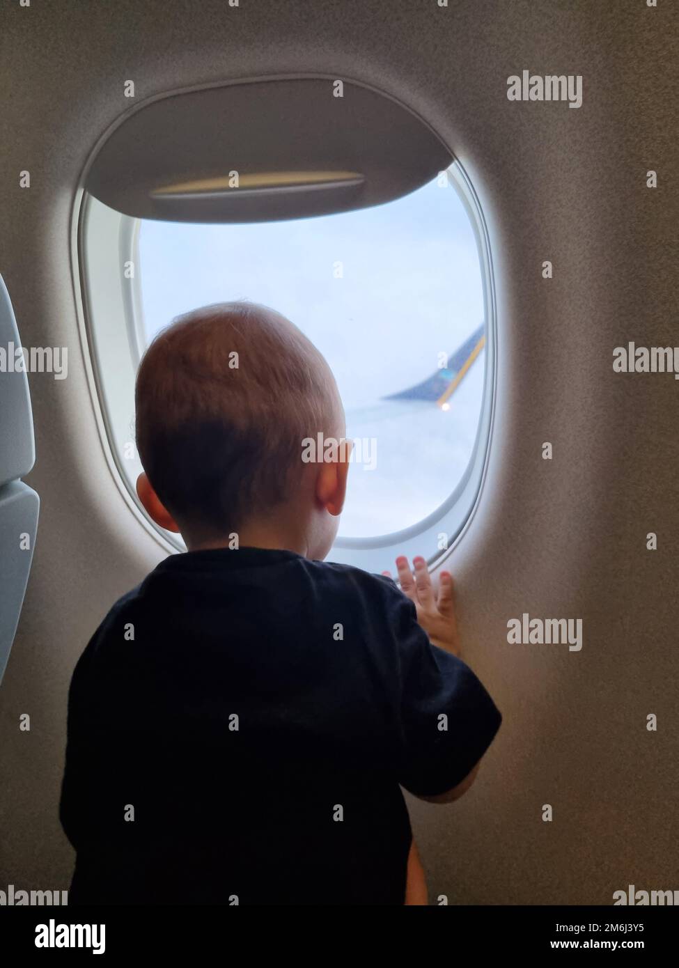 A vertical shot of a baby boy looking out of the window of an airplane ...