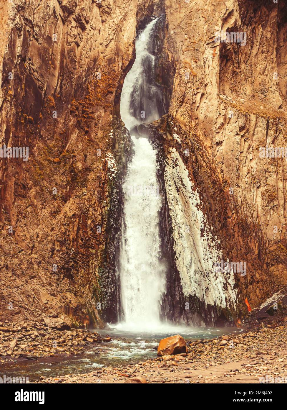The stream of a powerful waterfall flows down between the rocks into a ...