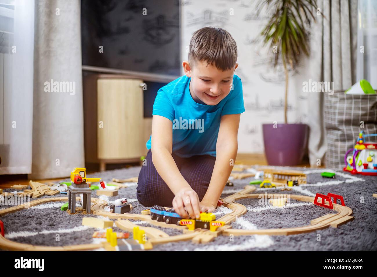Boy playing with toy train with wooden rails while sitting on floor at ...