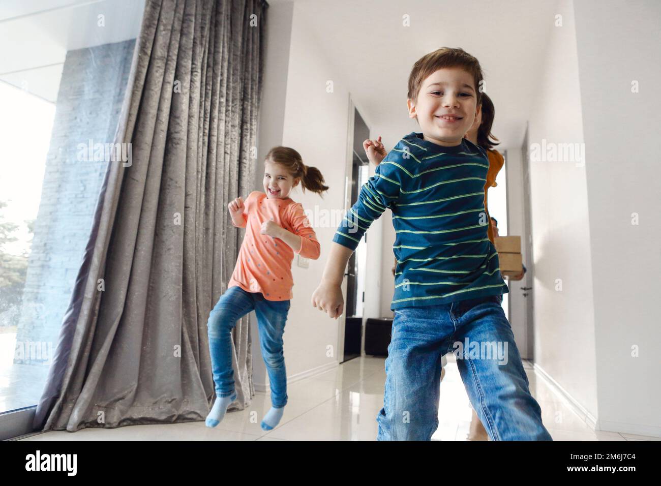 Happy family running in hall. Funny kids jumping with carton box ...