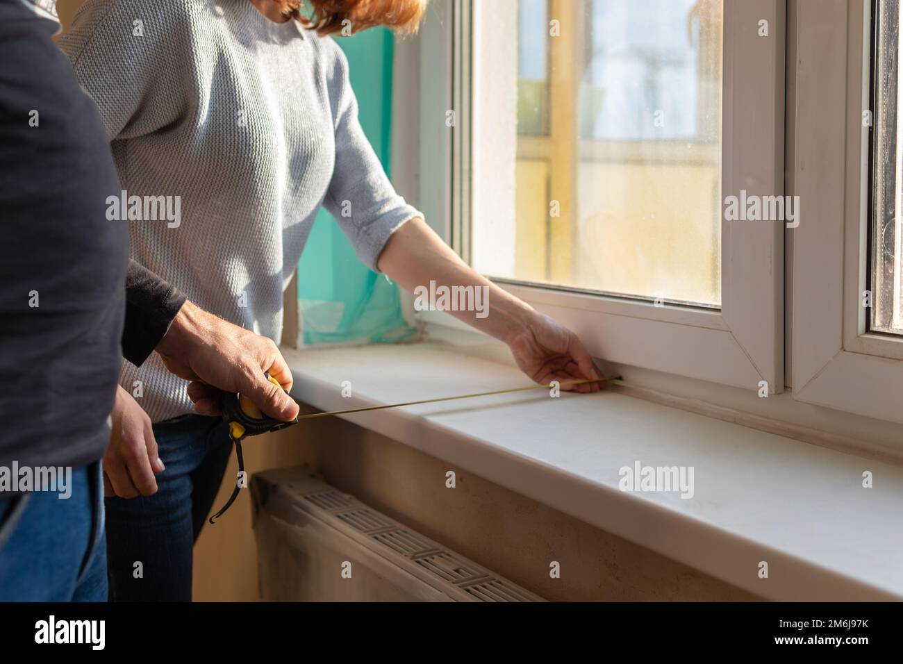 Young couple moving in new apartmen. People measure size of window sill ...