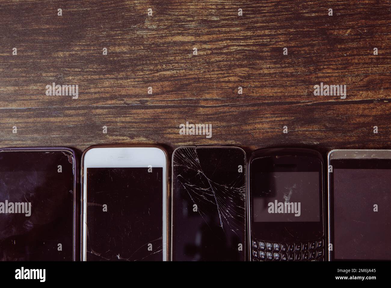 An assortment of outdated and damaged mobile phones with broken screens ...