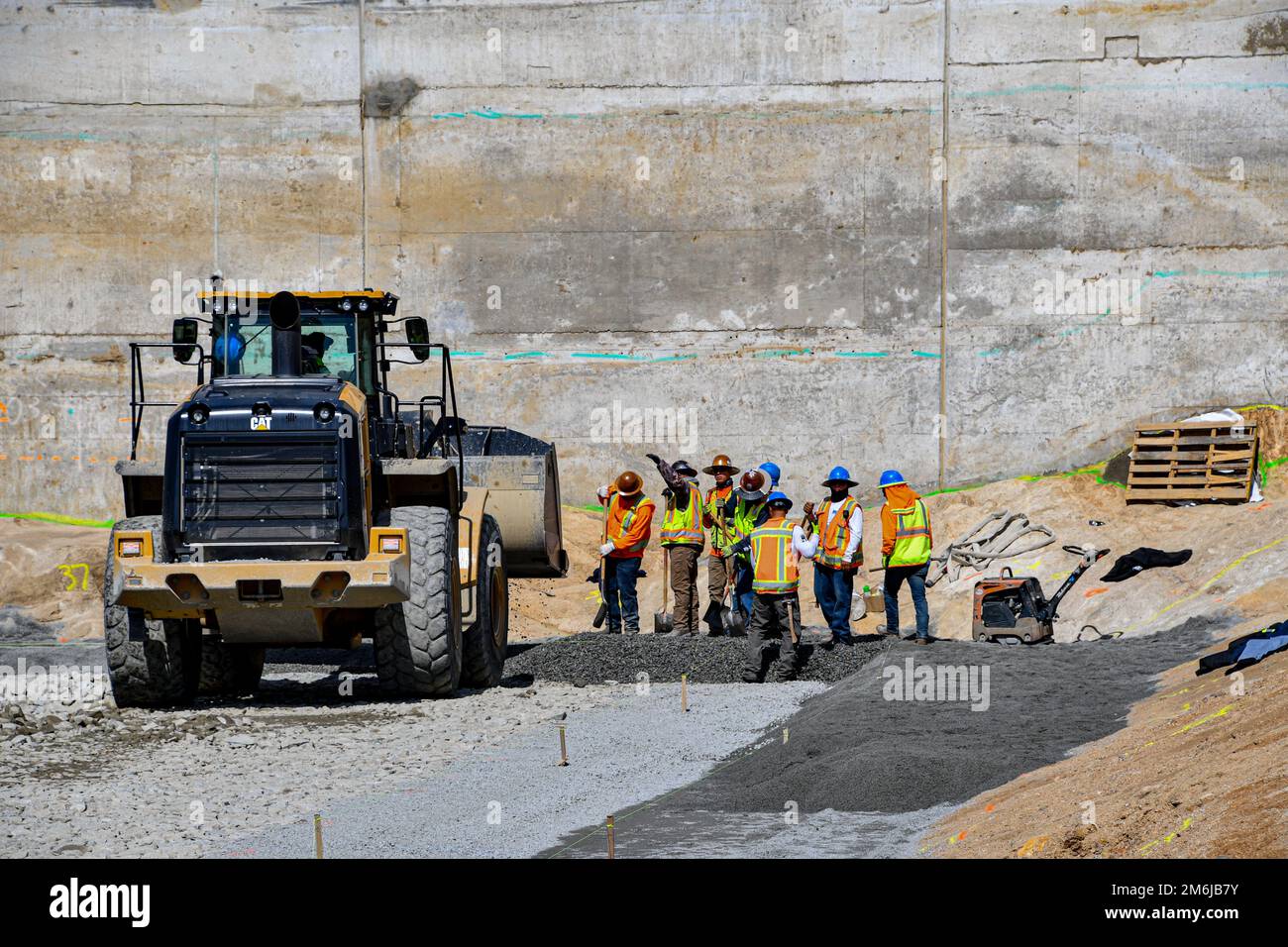 A front end loader carries drain rock to a crew of construction workers ...