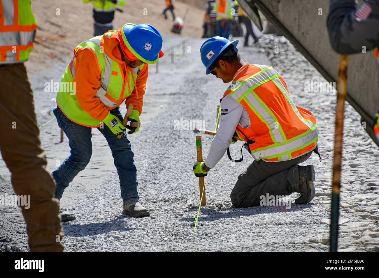 Workers mark a boundary to guide a front end loader dumping drain rock ...
